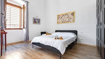 Quarto com cama, janela com cortinas, quadro na parede e mesa de cabeceira com abajur.