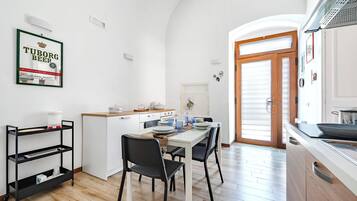 Uma cozinha moderna com área de refeições, apresentando uma mesa de madeira, cadeiras e um armário branco.