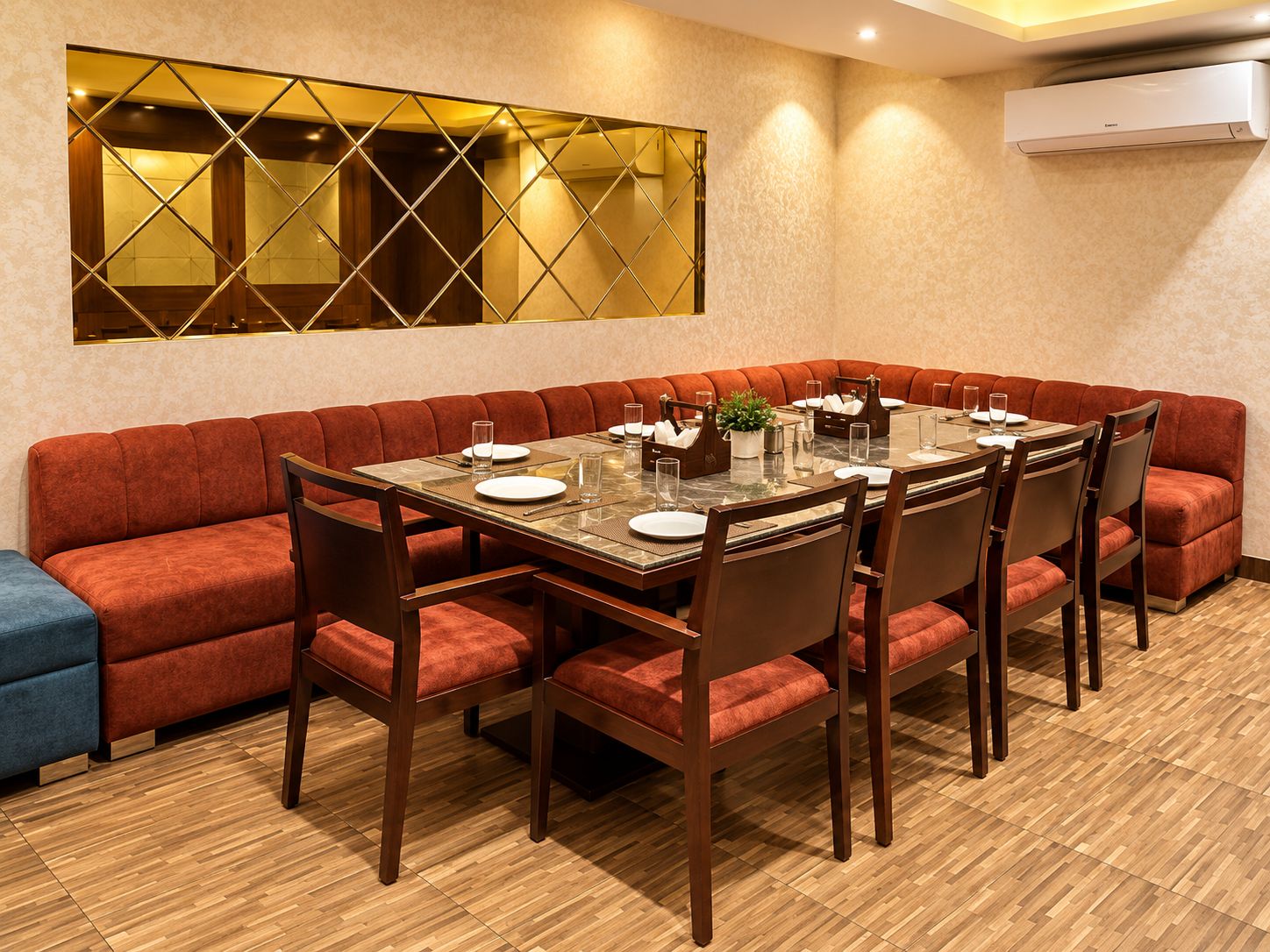 Uma sala de jantar com uma mesa retangular posta para seis pessoas, rodeada por sofás estofados vermelhos e cadeiras de madeira.