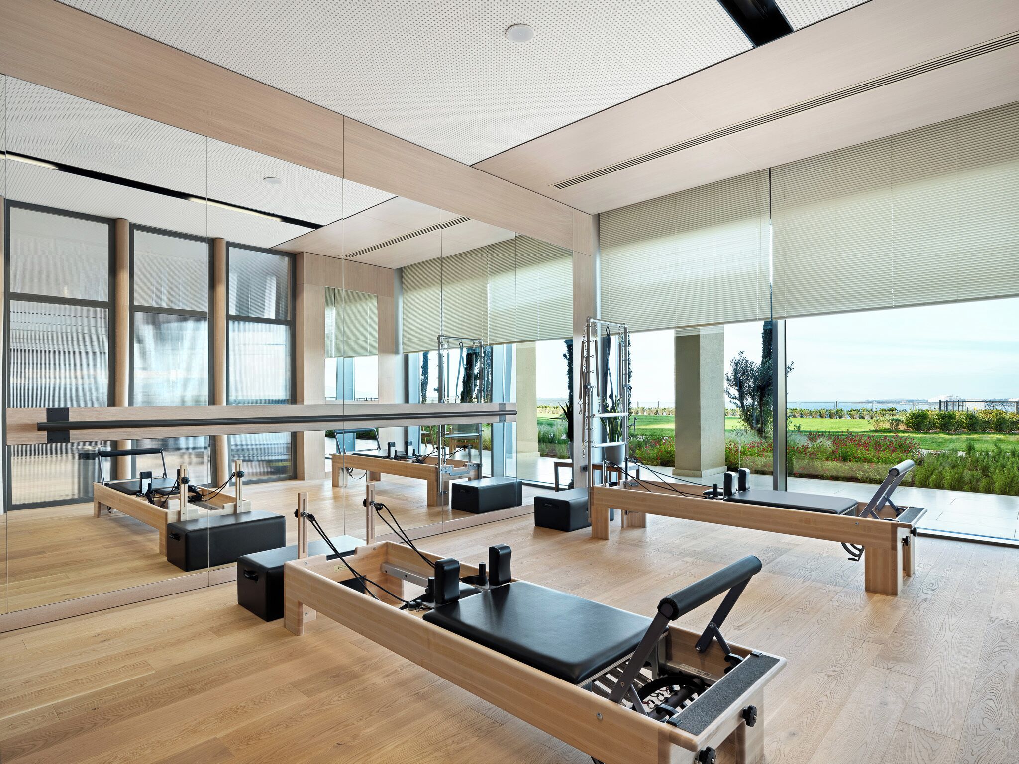 Um estúdio de Pilates com paredes espelhadas, piso de madeira e grandes janelas com vista para o exterior.