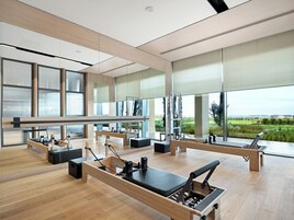 Um estúdio de Pilates com paredes espelhadas, piso de madeira e grandes janelas com vista para o exterior.