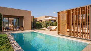 Uma piscina com espreguiçadeiras, um espaço com paredes de vidro e uma cerca de madeira.