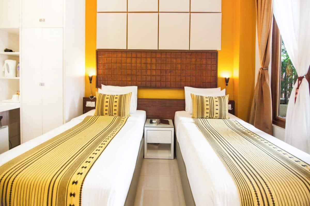 Quarto de hotel com duas camas, cabeceira de madeira, luminárias laterais e vista para o exterior.