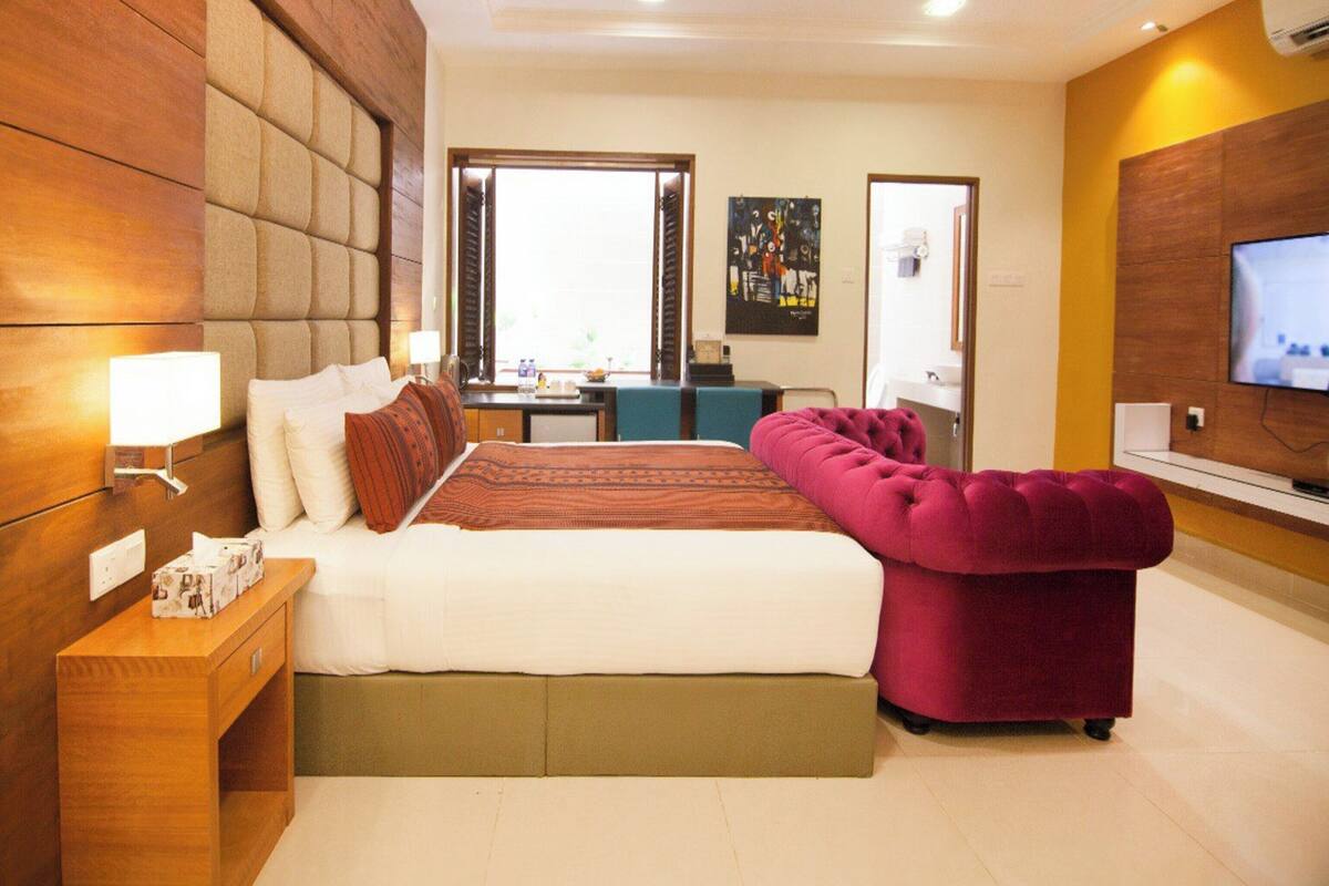 Quarto de hotel moderno com uma cama grande, uma escrivaninha, televisão e uma área de estar confortável.