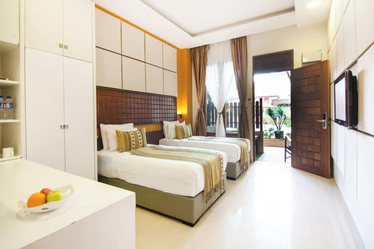 Quarto de hotel com duas camas, uma escrivaninha com uma fruteira e uma TV fixada na parede.