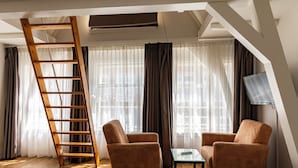 Quarto com escada de madeira, duas poltronas marrons, uma mesinha e uma cama.
