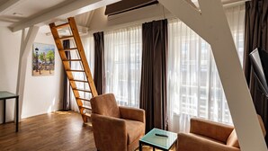 Uma sala de estar moderna com uma escada de madeira, uma poltrona marrom, uma mesa pequena e um quadro com uma paisagem urbana na parede.