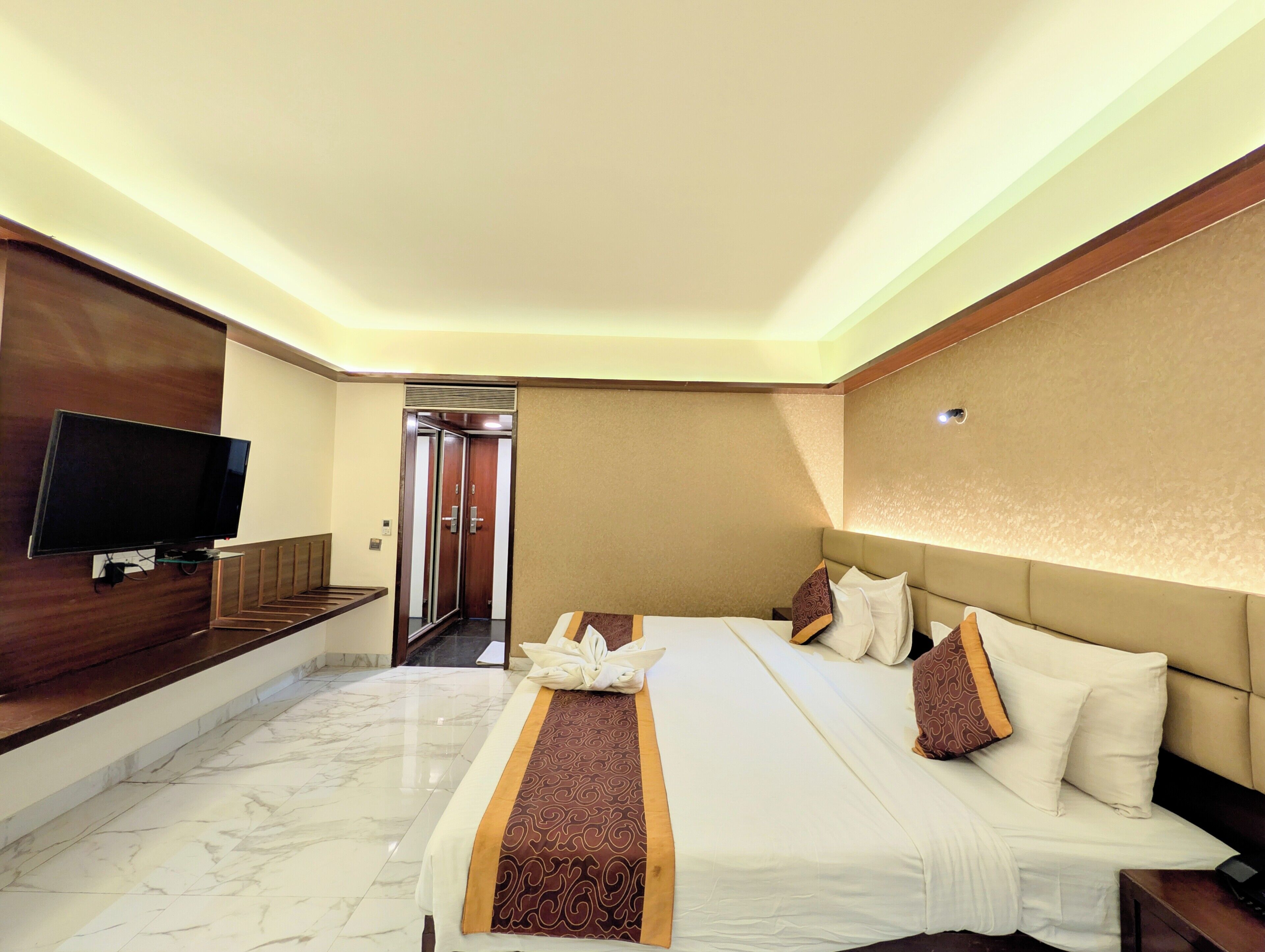 Quarto de hotel com cama, televisão, banheiro e corredor.