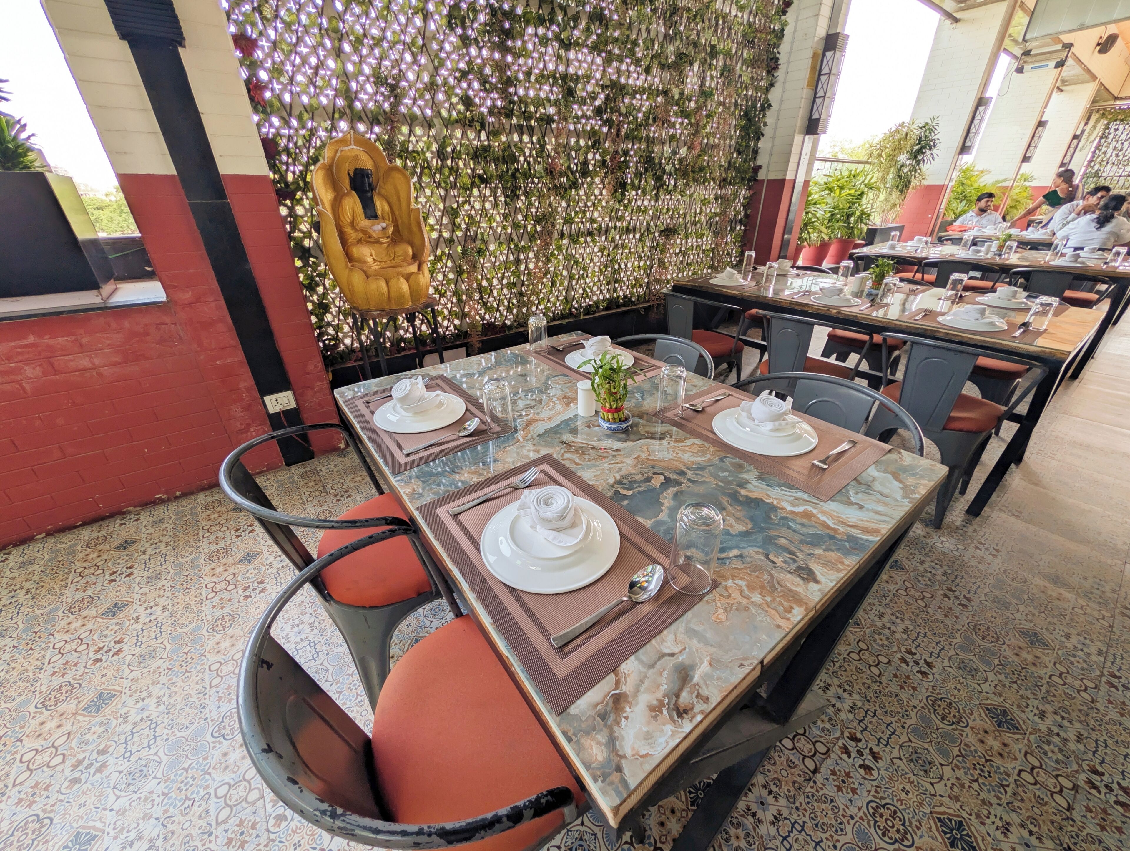 Restaurante com mesas de mármore, paredes vermelhas e pretas, e uma estátua decorativa de Buda.