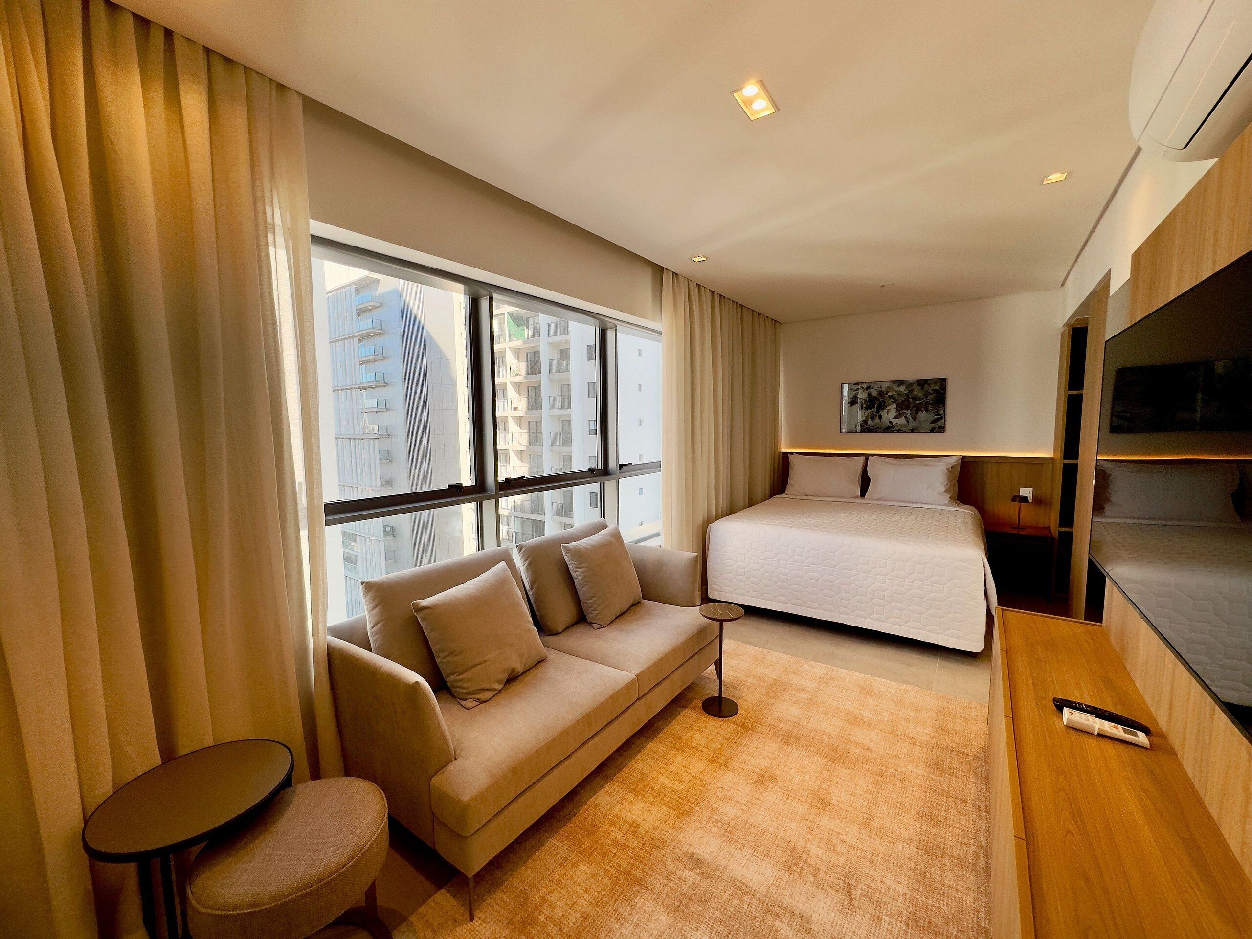 Quarto de hotel com sofá, mesa pequena, cama e televisão.