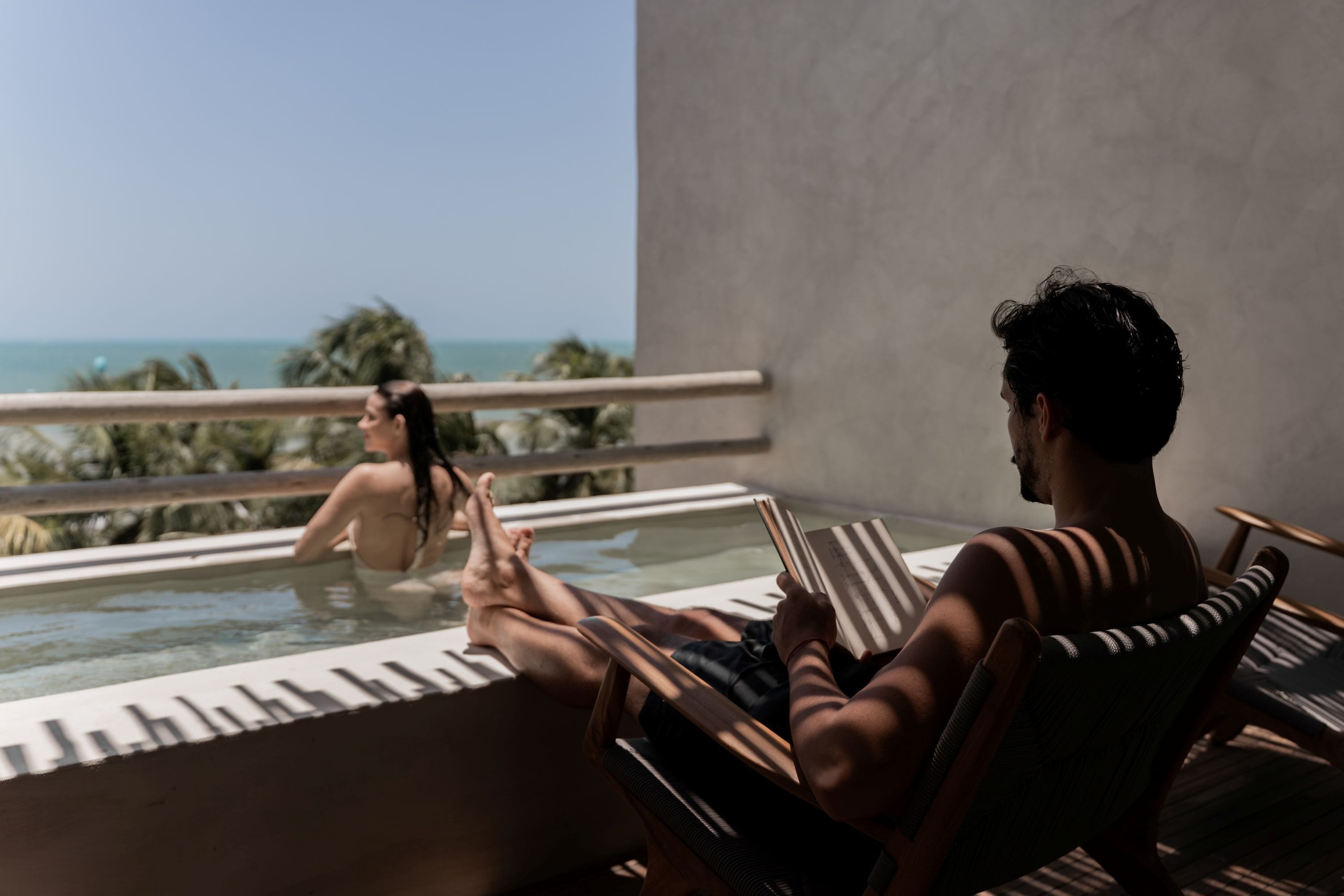 Uma pessoa relaxando à beira da piscina com vista para o oceano e palmeiras.