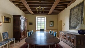 Uma sala de conferências com uma grande mesa redonda, cadeiras de madeira, um tapete estampado e vista para o exterior por uma grande janela.