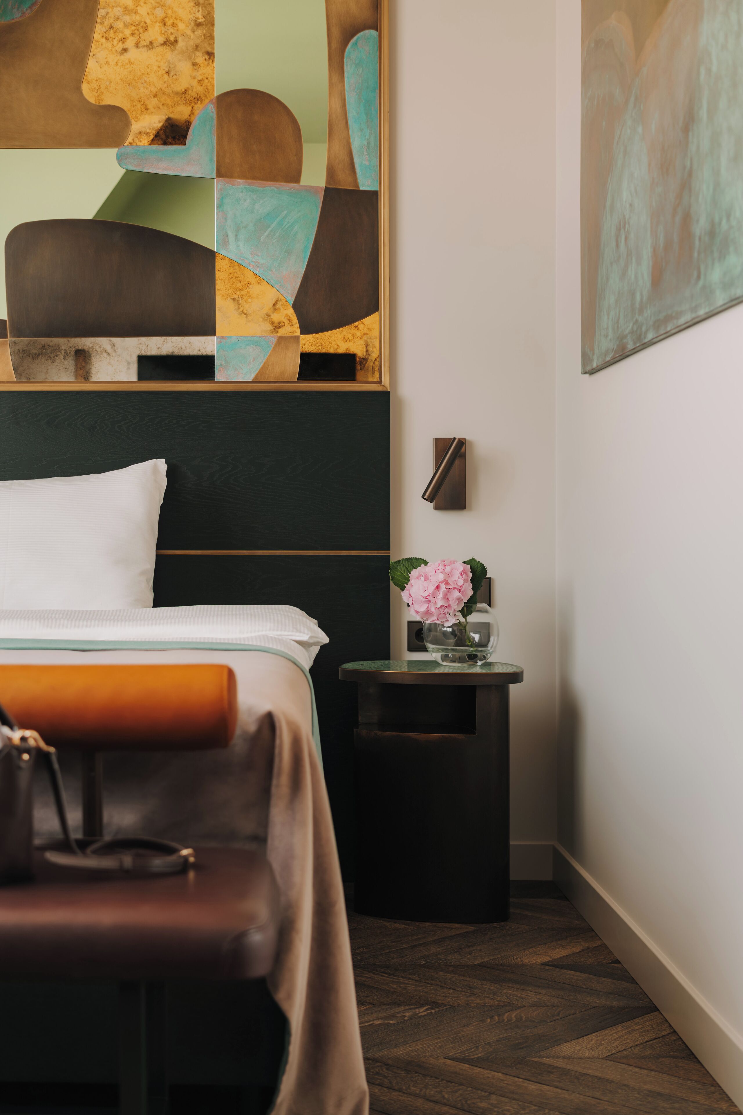 Quarto de hotel moderno com cama grande, mesa de cabeceira, vaso com flores e uma obra de arte na parede.