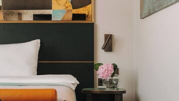 Quarto de hotel moderno com cama grande, mesa de cabeceira, vaso com flores e uma obra de arte na parede.