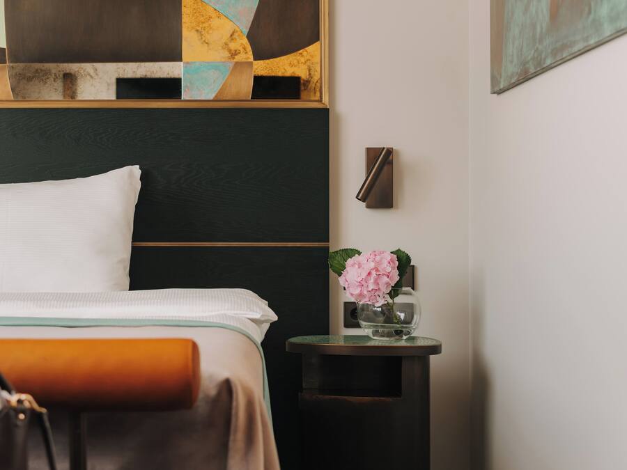 Quarto de hotel moderno com cama grande, mesa de cabeceira, vaso com flores e uma obra de arte na parede.