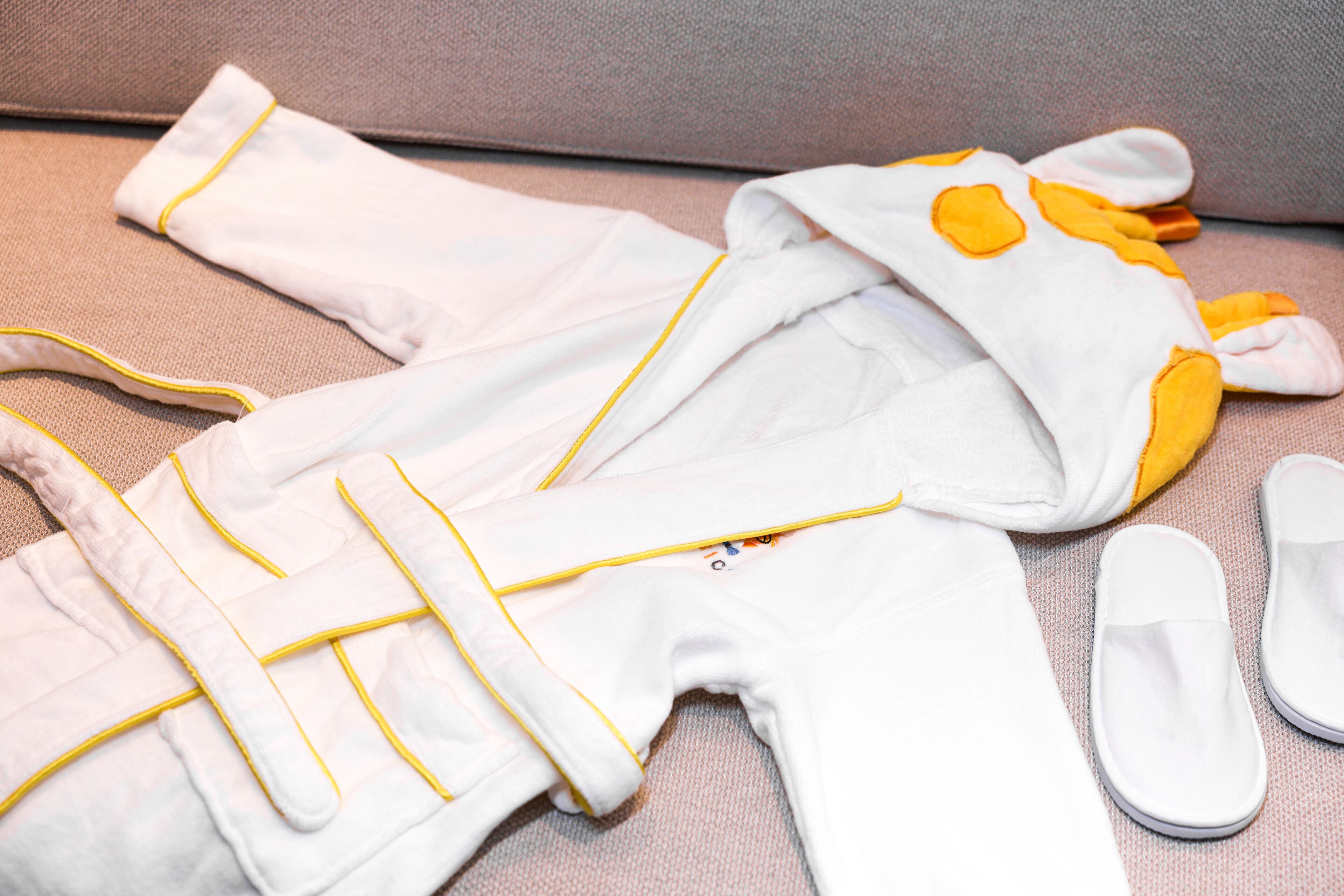 Um conjunto de pijama branco com detalhes amarelos e um brinquedo de pelúcia sobre uma superfície texturizada.