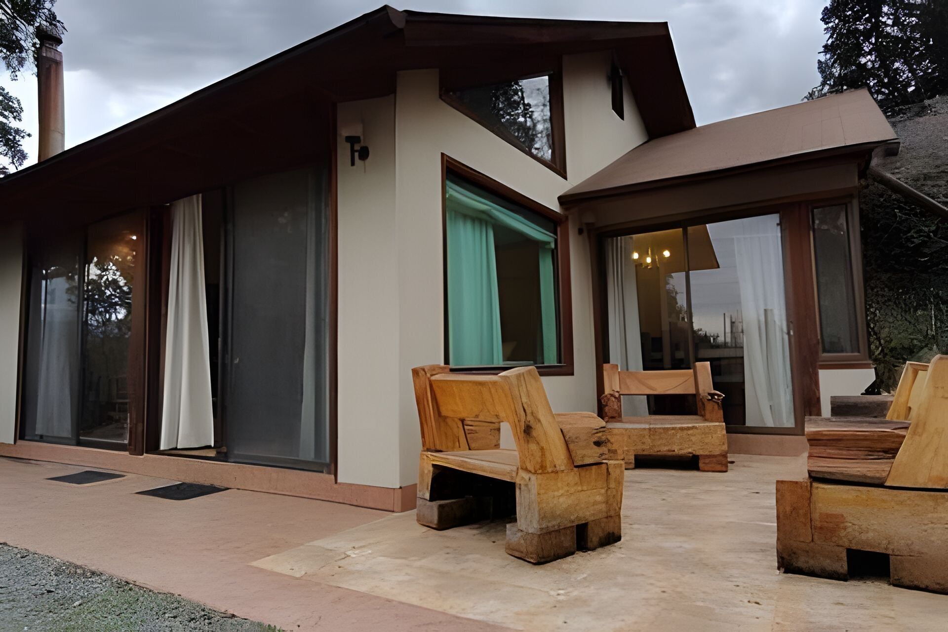 Uma casa moderna com grandes janelas, um pátio com móveis de madeira e uma chaminé.