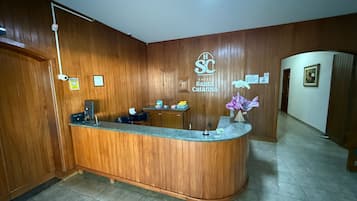 Balcão de recepção de hotel com acabamento em madeira, um logotipo acima do balcão e um arranjo de flores.