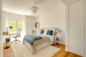 Quarto com cama, escrivaninha, cadeira, abajur e janela.