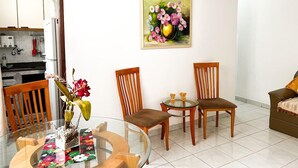 Uma sala de jantar com mesa de vidro, duas cadeiras de madeira, um sofá e um quadro de flores na parede.
