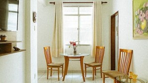 Quarto com ventoinha no teto, mesa de jantar com cadeiras, televisão na parede e janela com cortinas.