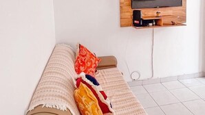 Um sofá bege com almofadas estampadas e uma televisão fixada na parede acima.