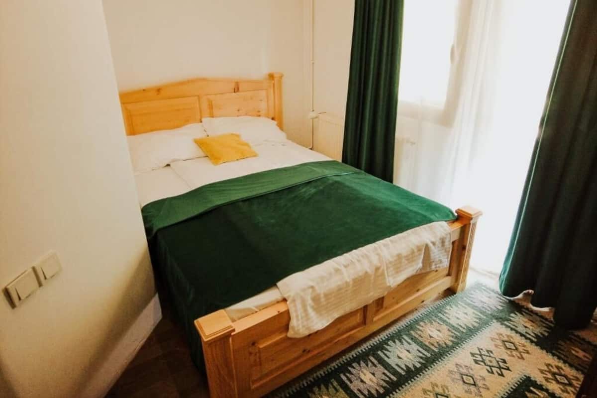 Uma cama de solteiro com cabeceira de madeira, colcha verde e manta branca.