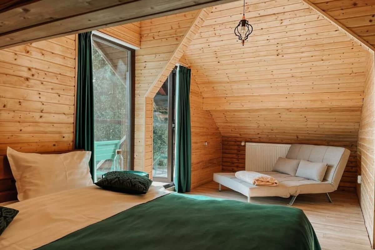 Quarto aconchegante com painéis de madeira, uma cama, um sofá e uma grande janela.