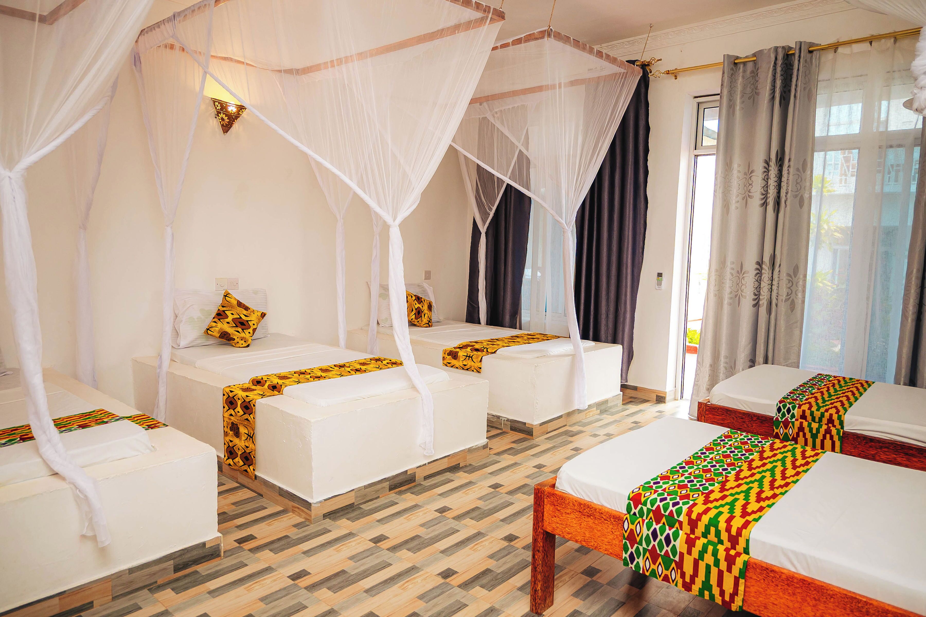 Quarto de hotel com quatro camas, cada uma com dossel, e uma janela grande com cortinas.
