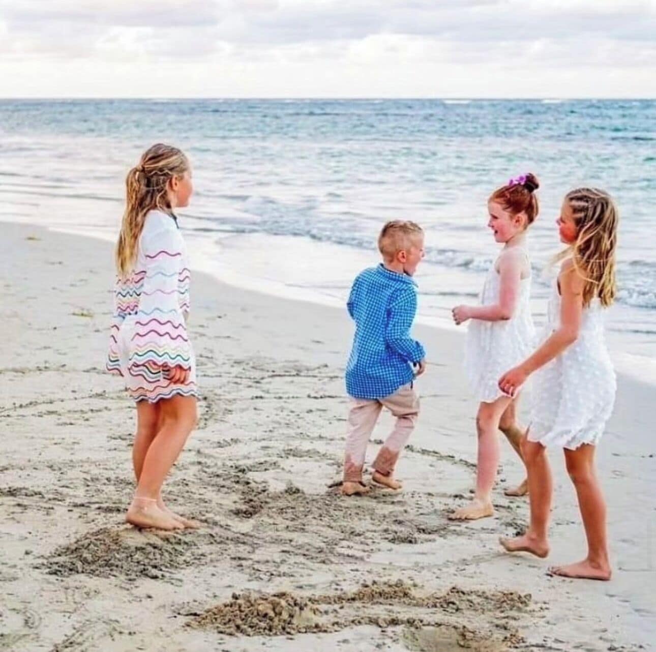 Um grupo de crianças brincando em uma praia de areia, com o oceano ao fundo.