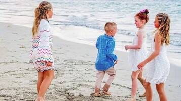Um grupo de crianças brincando em uma praia de areia, com o oceano ao fundo.