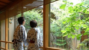 Decoração tradicional japonesa com teto de madeira, uma grande janela de vidro e vista para o verde lá fora.