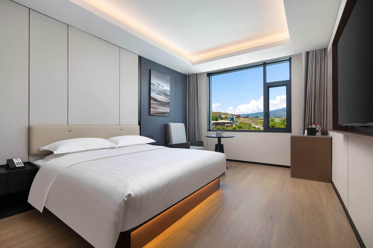 Quarto de hotel moderno com uma cama grande, uma escrivaninha e vista para as montanhas.