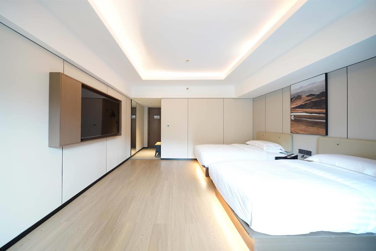 Quarto de hotel moderno com uma cama grande, uma TV fixada na parede e um quadro com uma paisagem.