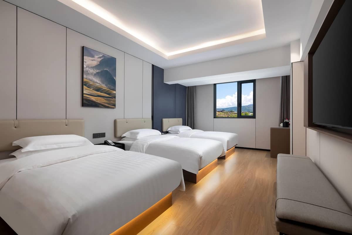 Quarto de hotel com duas camas, um sofá, uma televisão e uma grande janela com vista para a montanha.