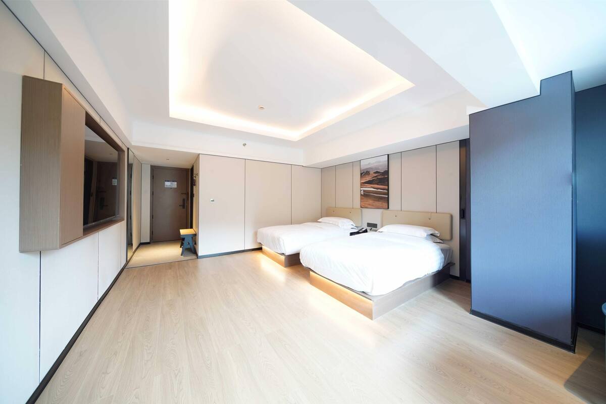 Quarto de hotel moderno com duas camas, um espelho grande e vista para as montanhas.