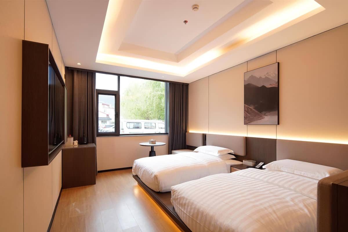 Quarto de hotel com duas camas, uma mesinha, televisão e janela com vista para um veículo do lado de fora.