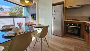 Cozinha moderna com mesa de jantar de vidro, eletrodomésticos de aço inoxidável e vista para o exterior.