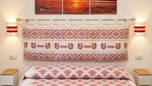 Quarto com colcha estampada, cabeceira decorativa e pintura de pôr do sol acima da cama.