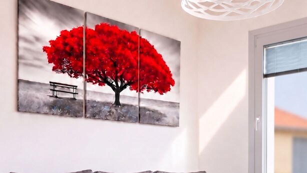 Uma sala de estar moderna com um sofá cinzento, almofadas estampadas em vermelho, uma mesa branca com uma tigela vermelha e uma cadeira vermelha. Um quadro grande de uma árvore vermelha está na parede.