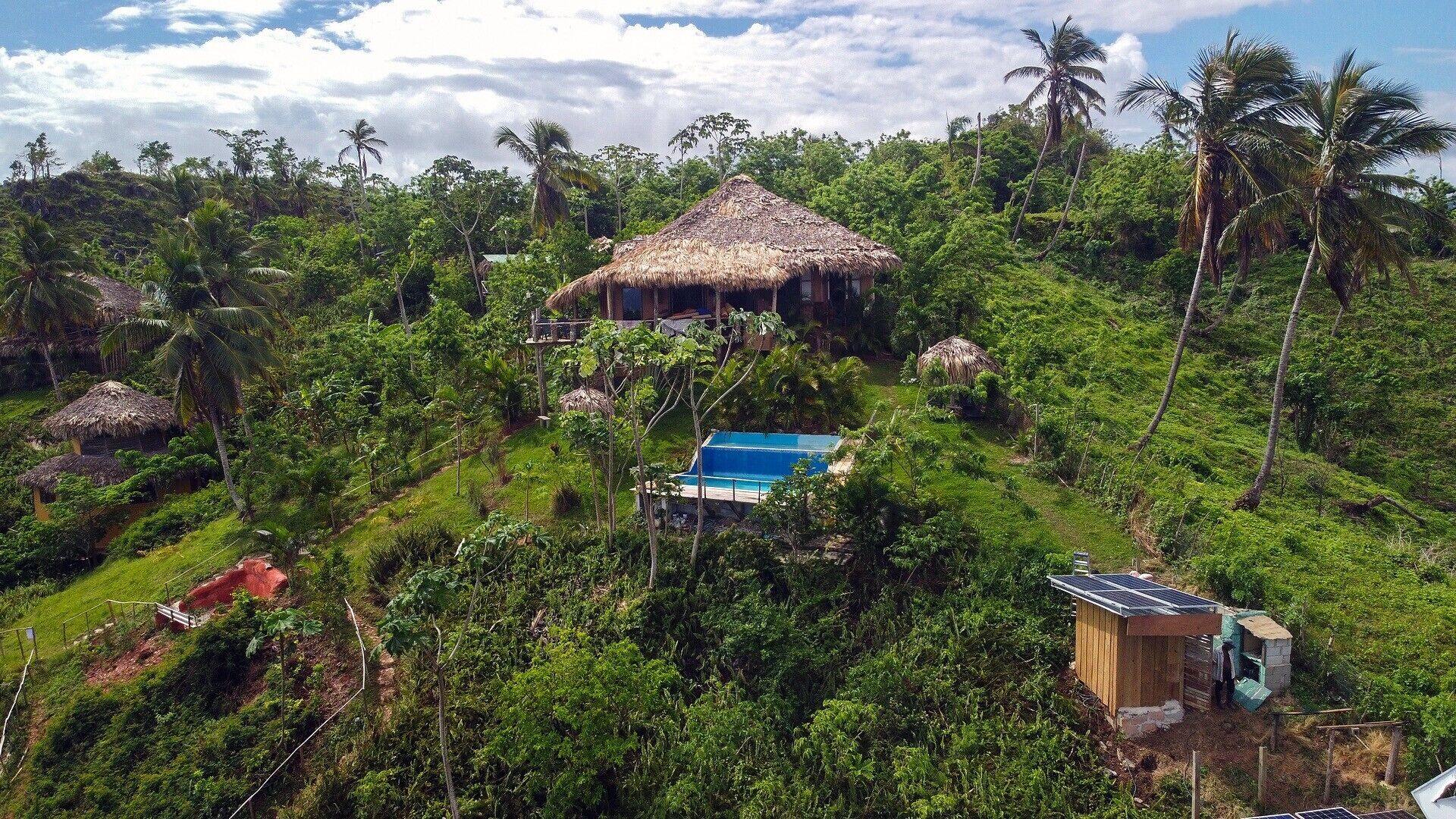 Paisagem rural com cabanas de palha rodeadas por vegetação exuberante e palmeiras.