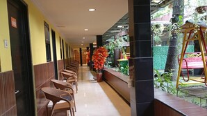 Corredor de hotel com cadeiras de vime, um banco e um vaso com flores laranjas.