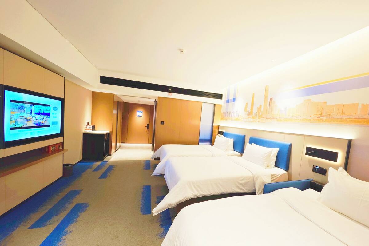 Quarto de hotel com duas camas, televisão na parede e uma pintura com vista para a cidade.