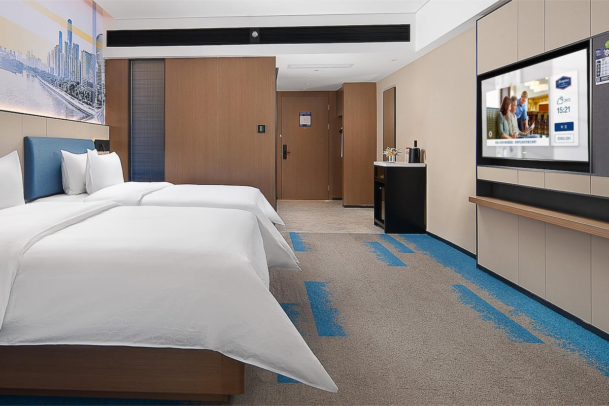 Quarto de hotel com uma cama grande, televisão e uma pintura com vista para a cidade.