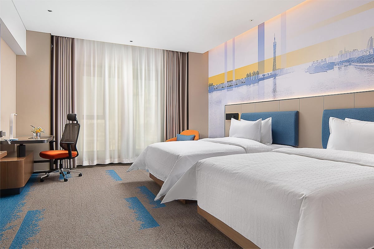 Quarto de hotel com duas camas, uma escrivaninha e uma cadeira.