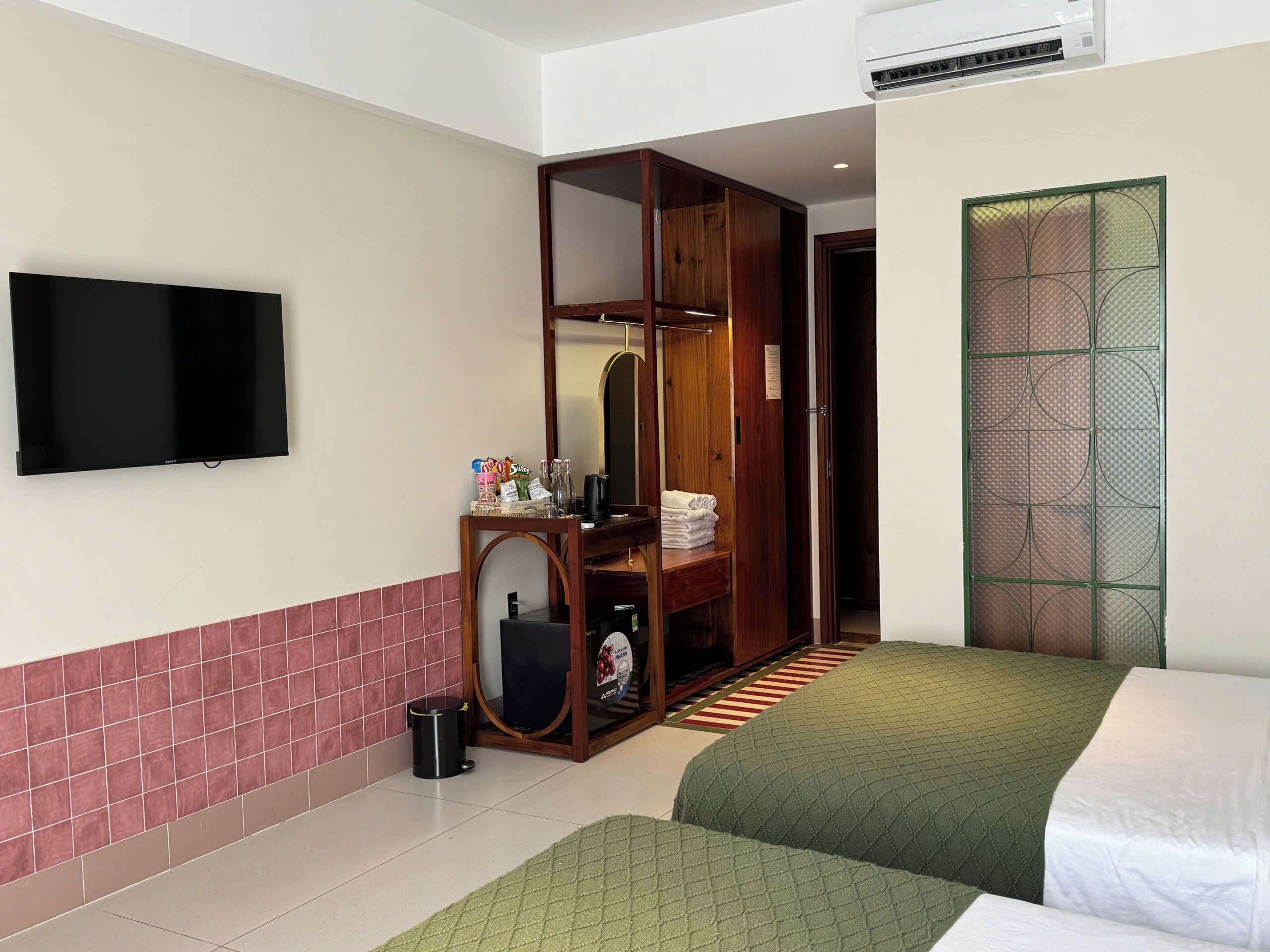 Quarto de hotel com televisão, guarda-roupa de madeira, cama e colcha verde.