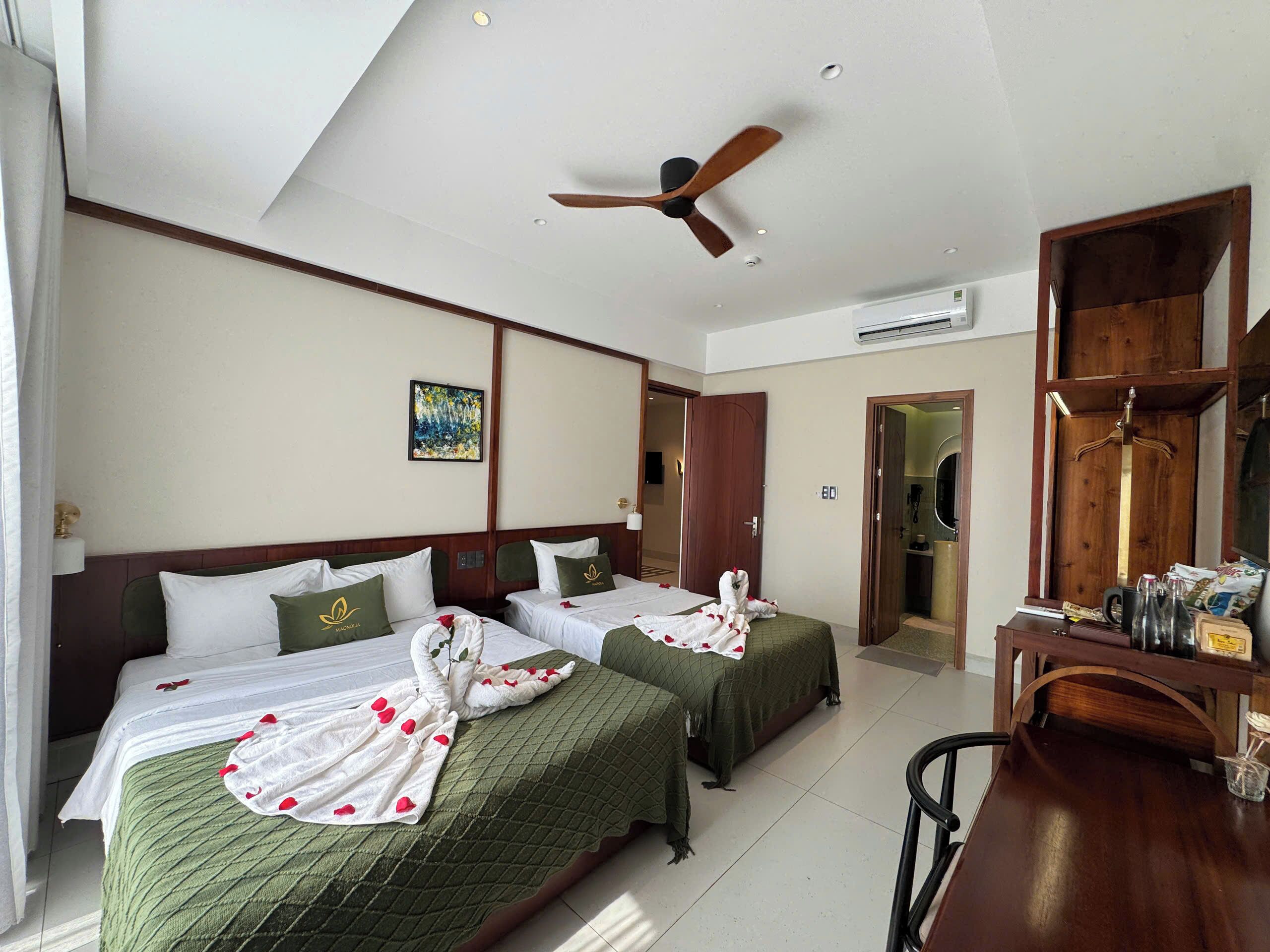 Quarto de hotel com duas camas, um ventilador de teto, um aparelho de ar condicionado, um quadro na parede e um guarda-roupa de madeira.