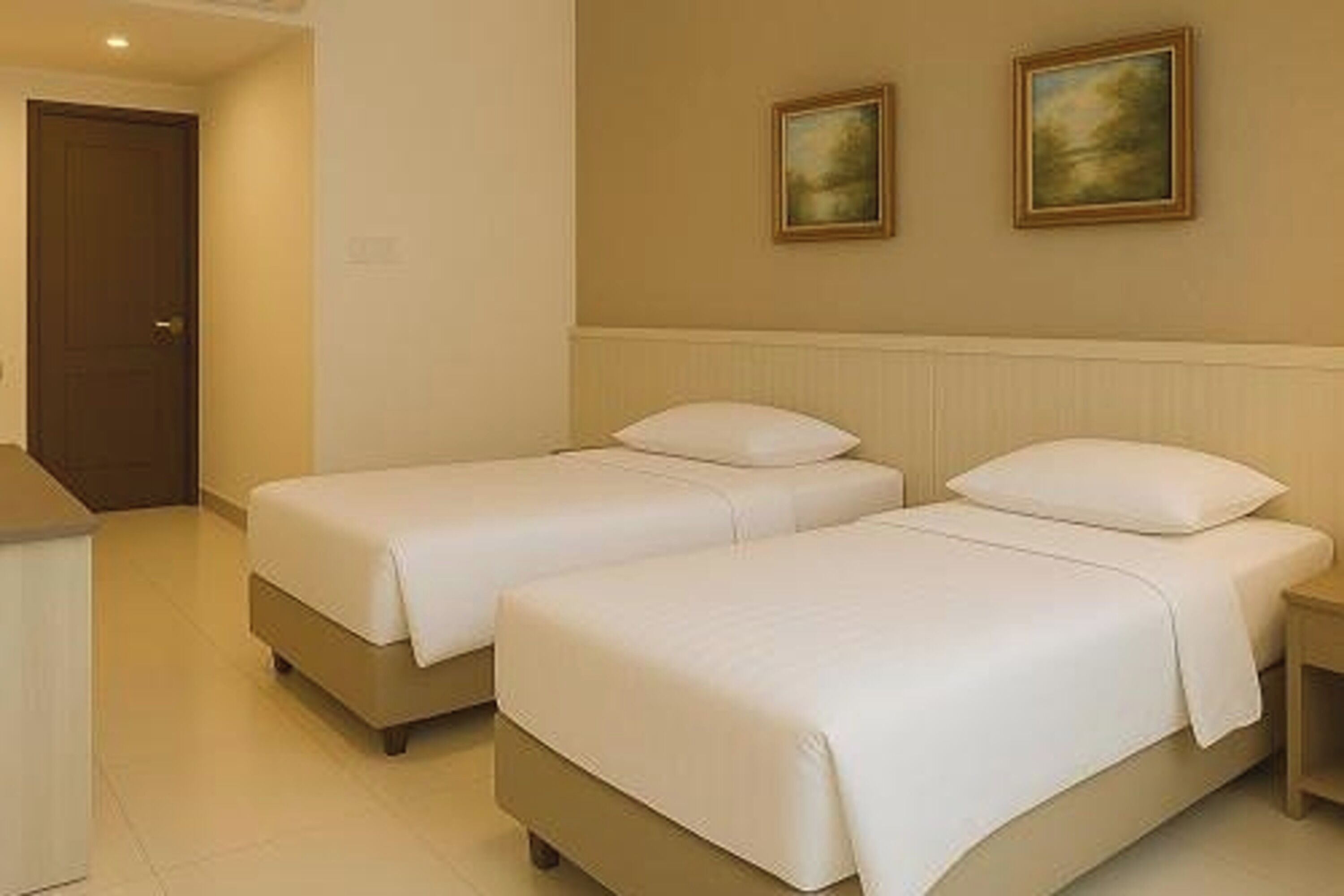 Quarto de hotel com duas camas, uma porta e duas pinturas na parede.