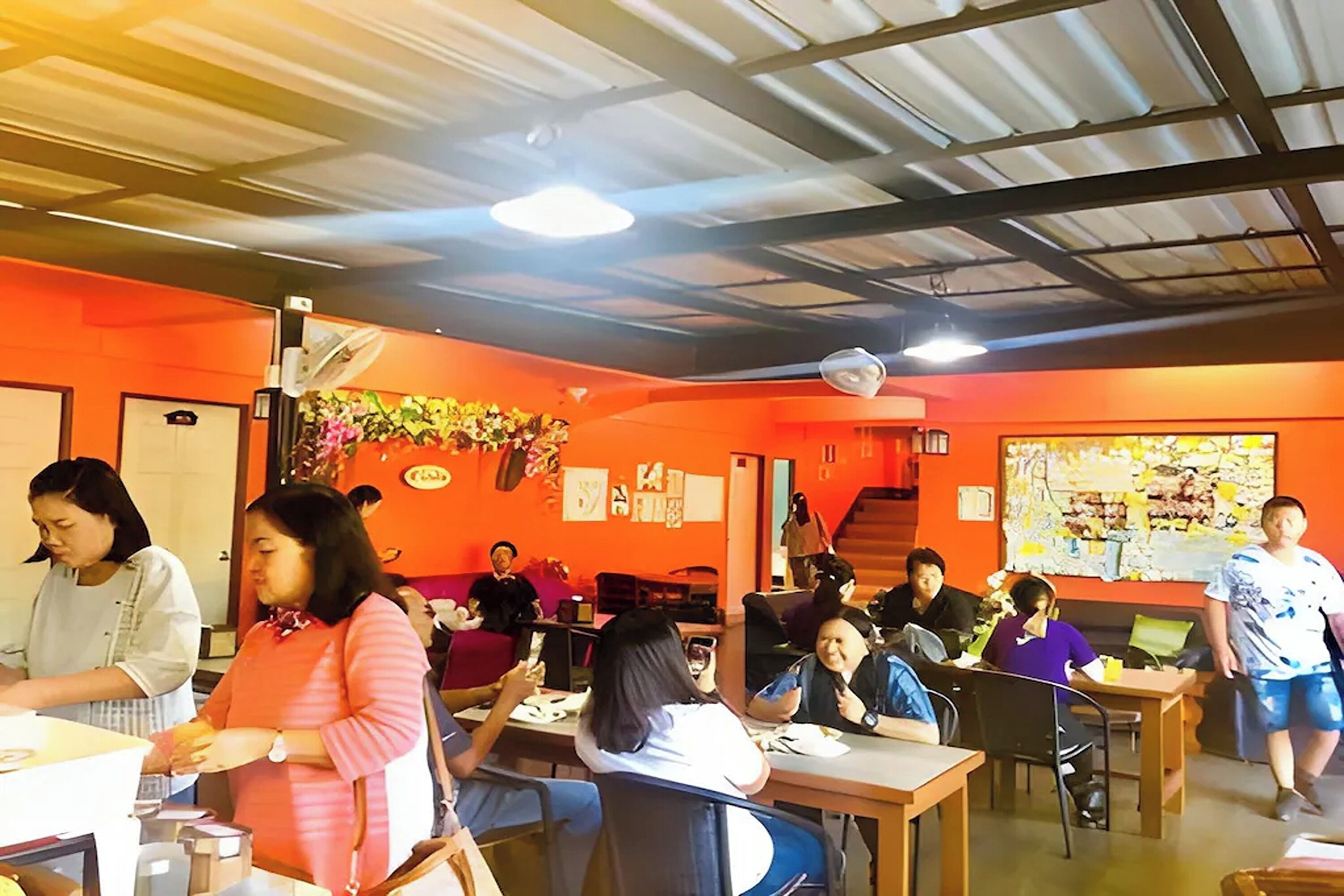 Restaurante com teto alto e paredes alaranjadas, com mesas e cadeiras para refeições.