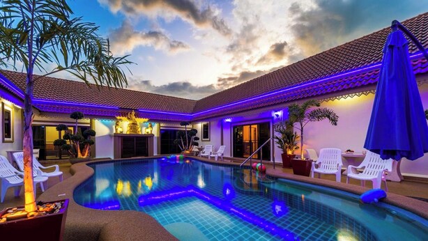 Piscina com deck ladrilhado, rodeada por cadeiras de praia e guarda-sóis, sob um céu ao pôr do sol.